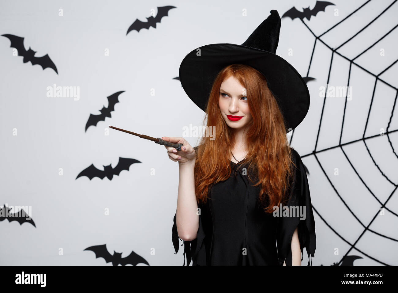 Halloween Concept - Beautiful Witch playing with magic stick on grey ...