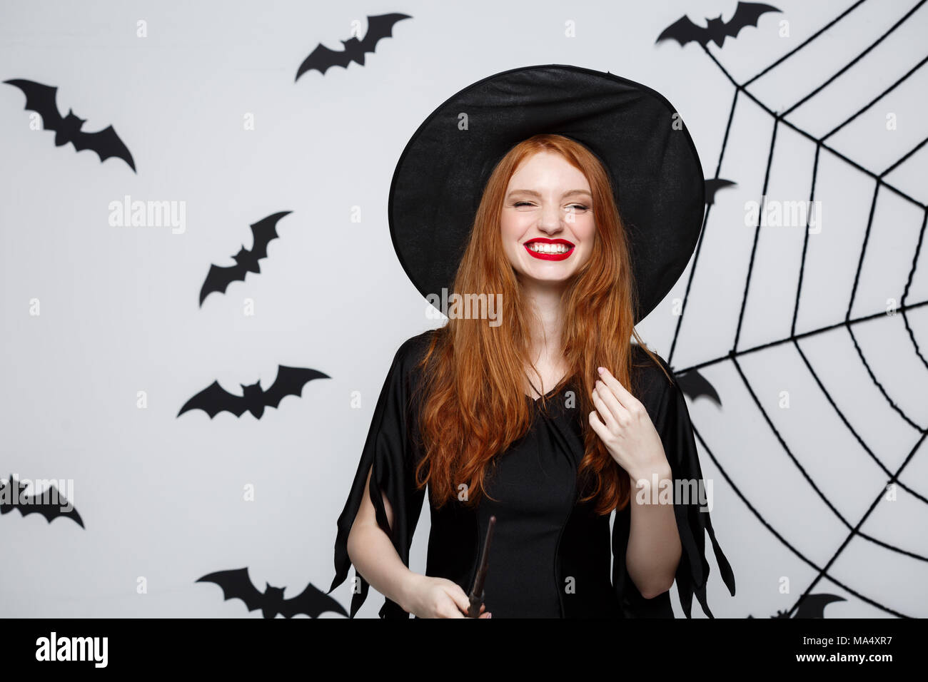 Halloween Concept - Beautiful Witch playing with magic stick on grey ...