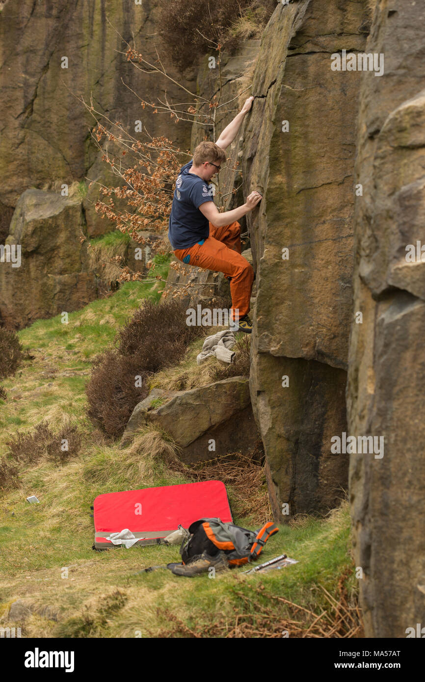 young man rock climbing (bouldering) without ropes on brownish rock ...