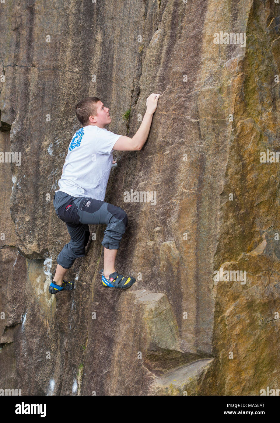 young man rock climbing (bouldering) without ropes on brownish rock ...