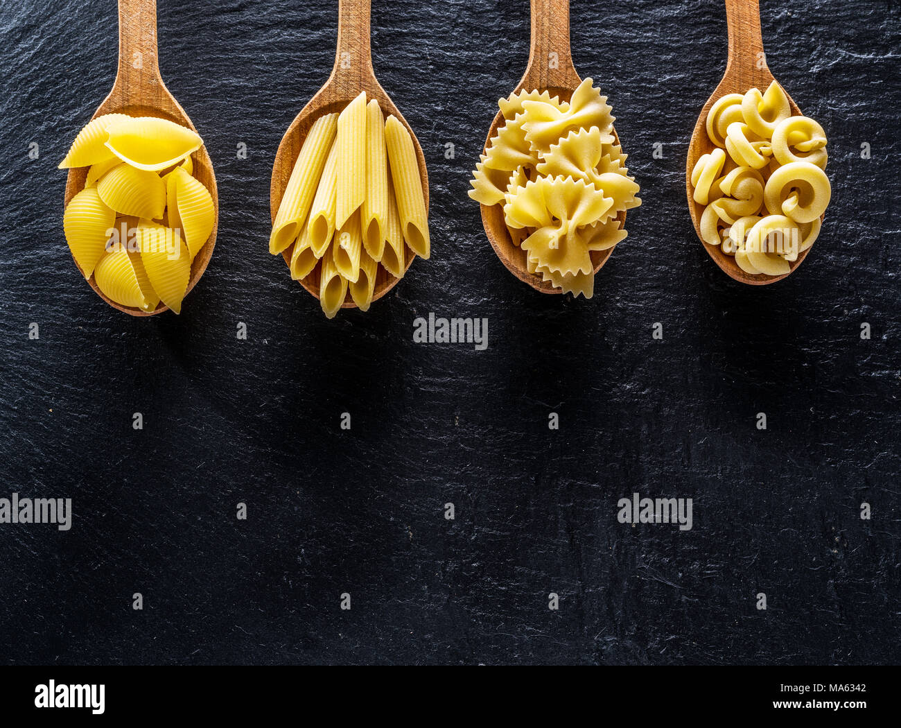 Different pasta types in wooden spoons on the table. Top view Stock ...