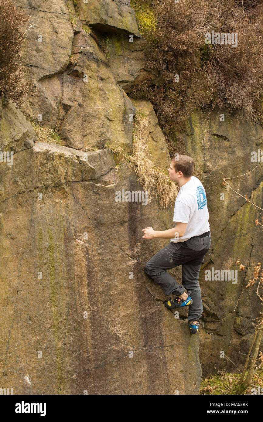 young man rock climbing (bouldering) without ropes on brownish rock ...