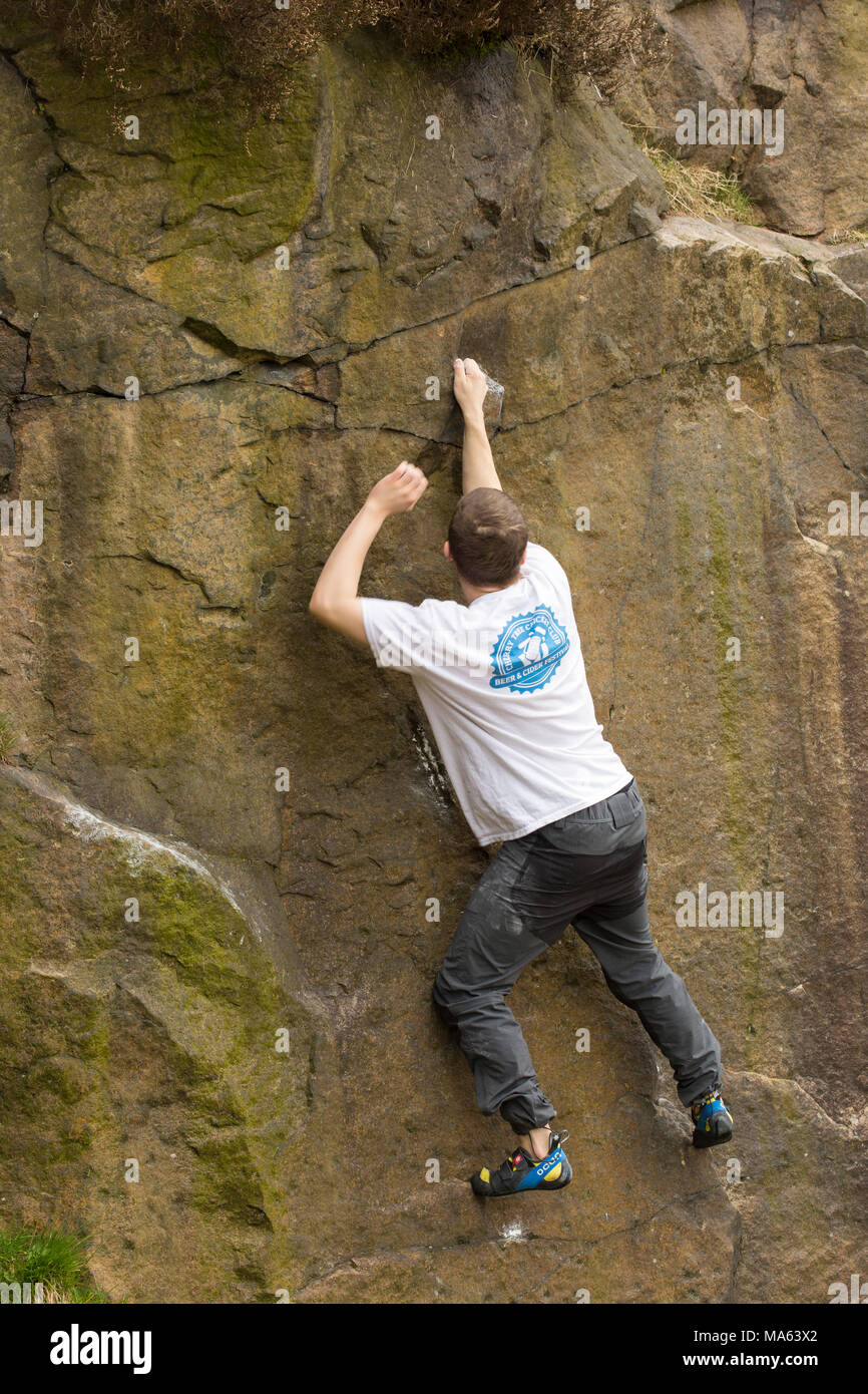 young man rock climbing (bouldering) without ropes on brownish rock ...