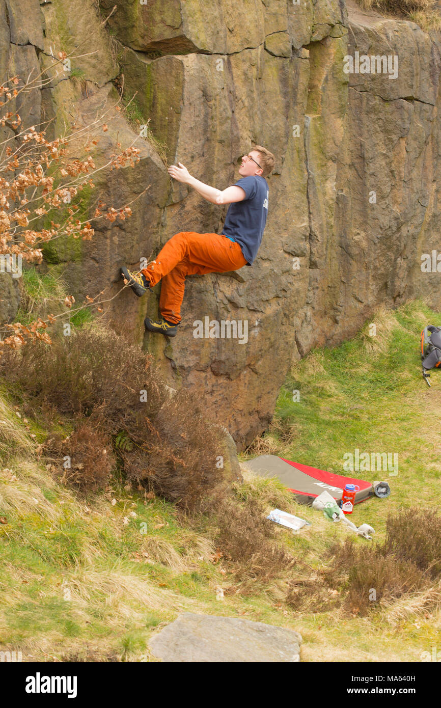 young man rock climbing (bouldering) without ropes on brownish rock ...