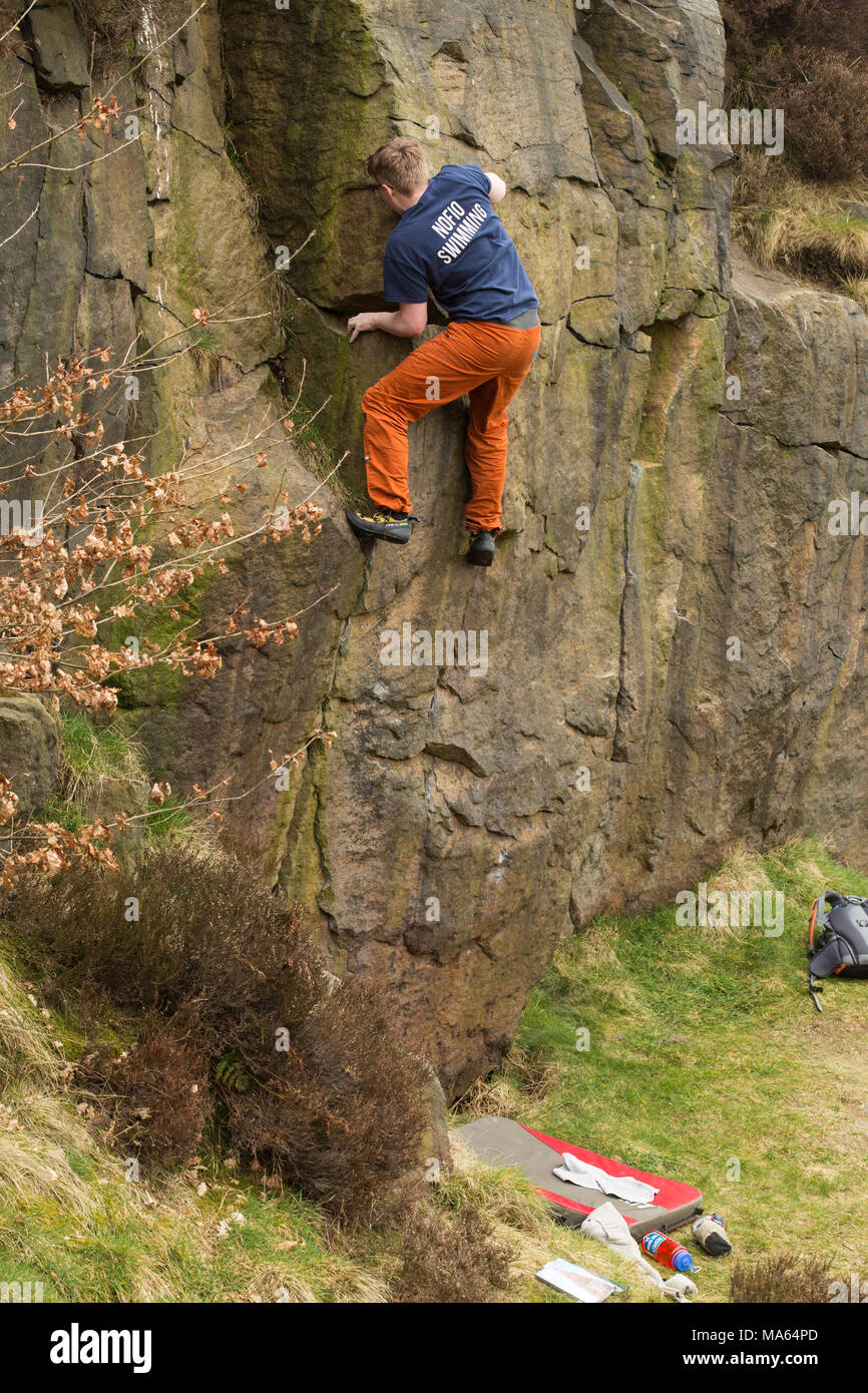 young man rock climbing (bouldering) without ropes on brownish rock ...