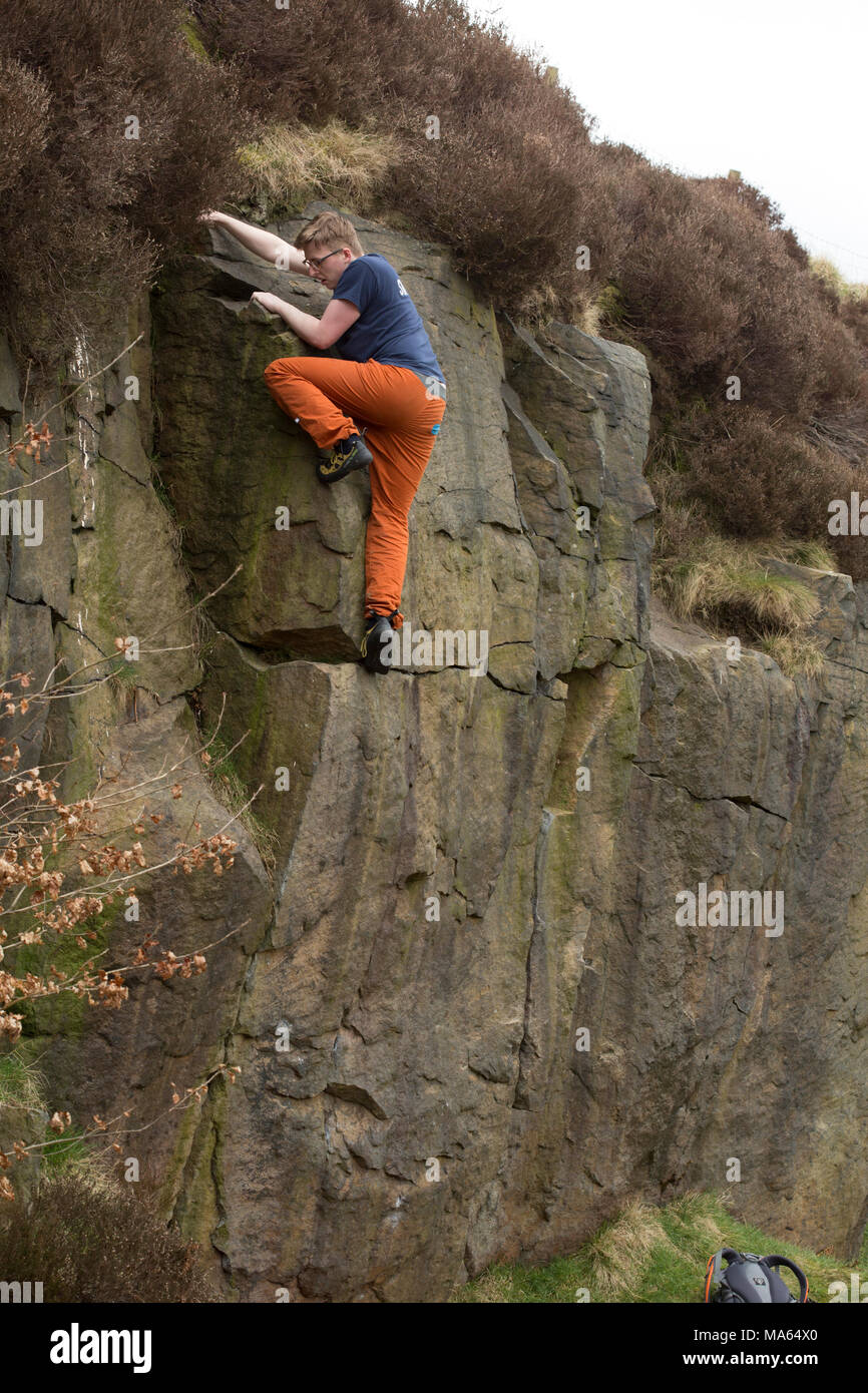 young man rock climbing (bouldering) without ropes on brownish rock ...
