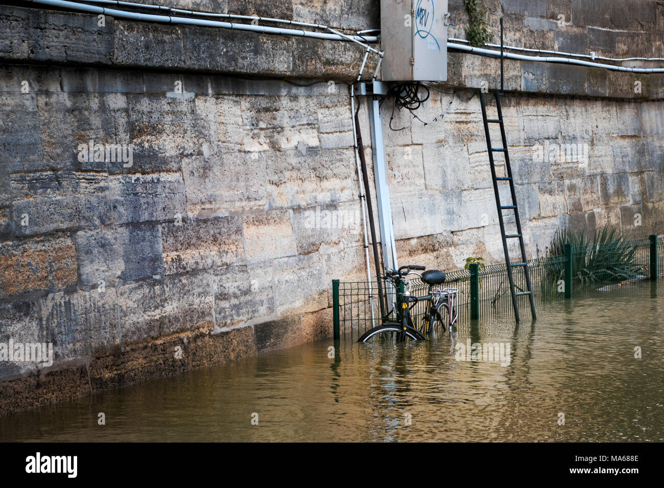 Bicycle secured to fencing submerged on a sunken pathway in the swollen ...