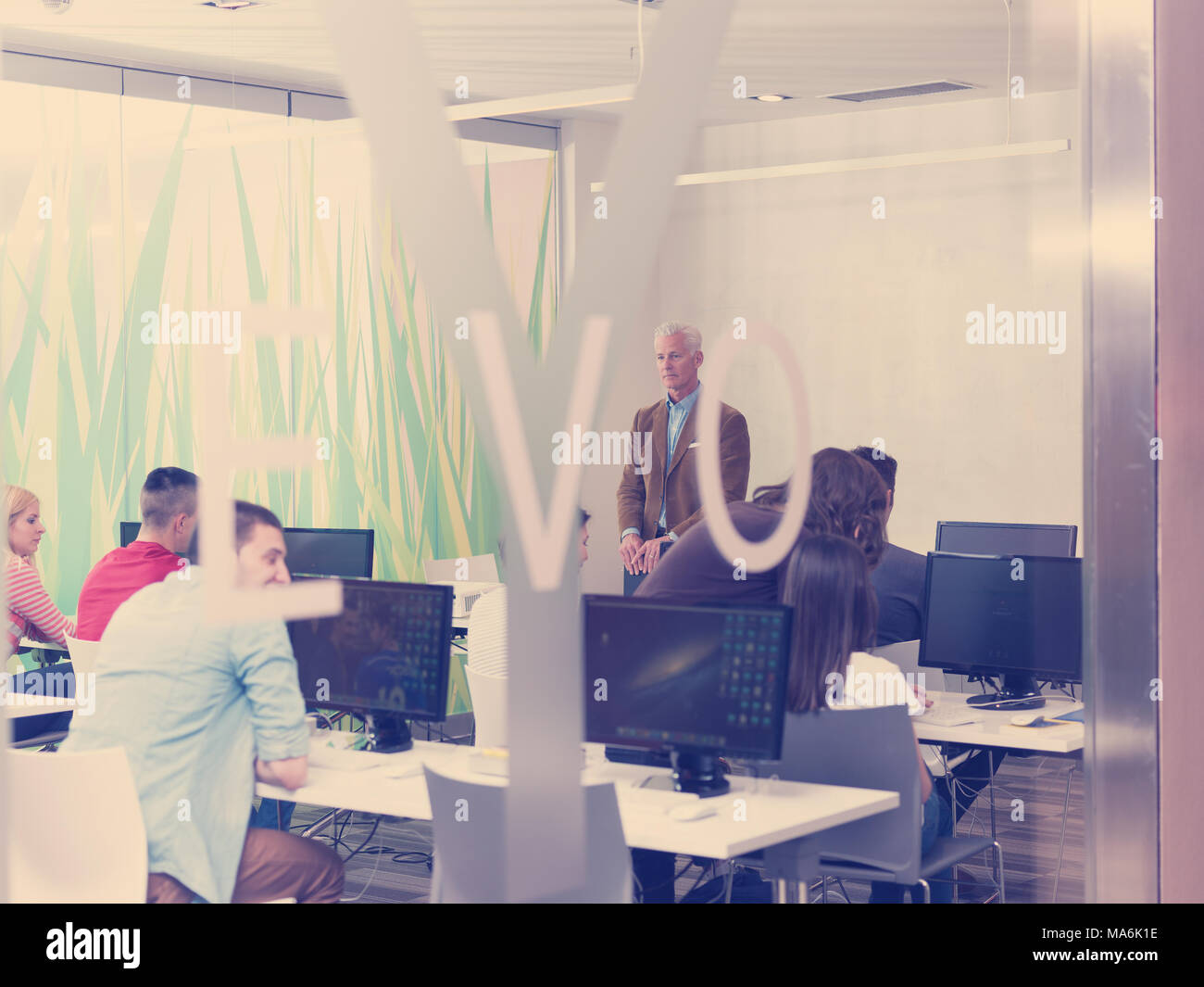 Handsome senior teacher and students group in computer lab classroom ...