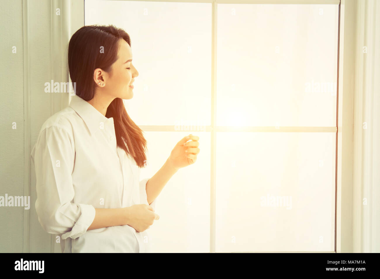 Beautiful young woman looking out in window at home and smiley so happy ...