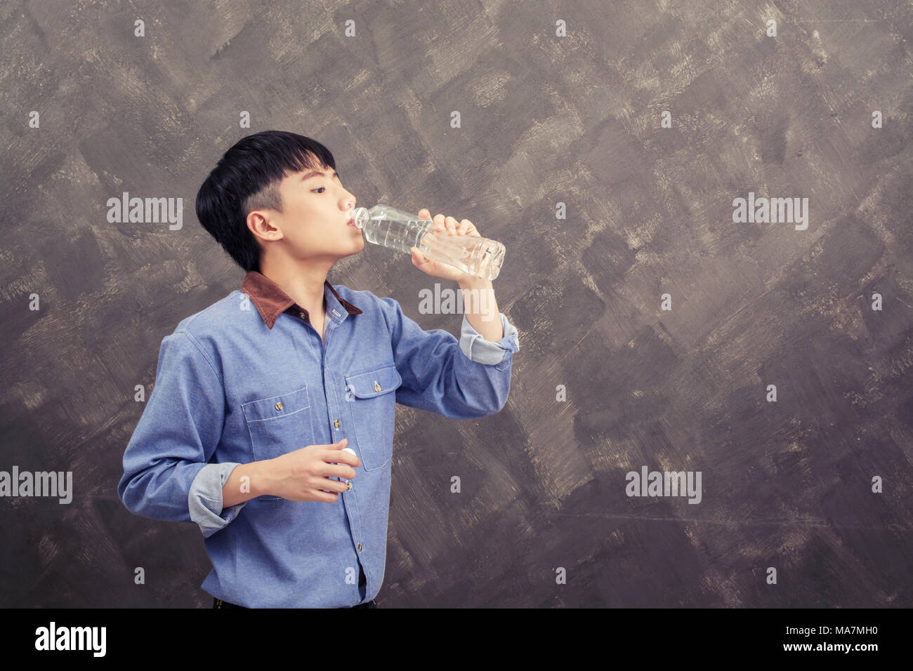 Handsome young asian man drinking water in front of grunge background ...