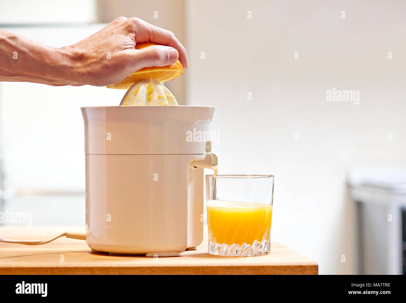 Hand pressing orange fruit with electric juicer in a modern kitchen ...