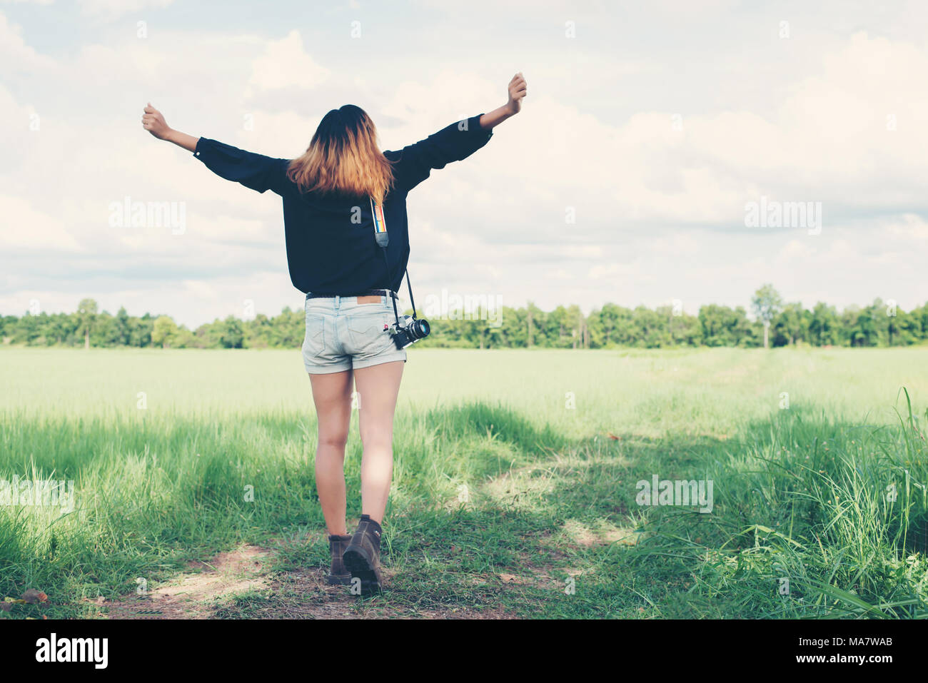Back of young woman carrying retro camera in grass field enjoy to go ...