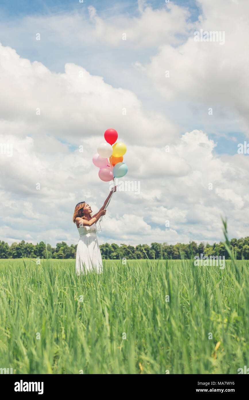 Happy young beautiful woman holding balloons in the grass field enjoy ...