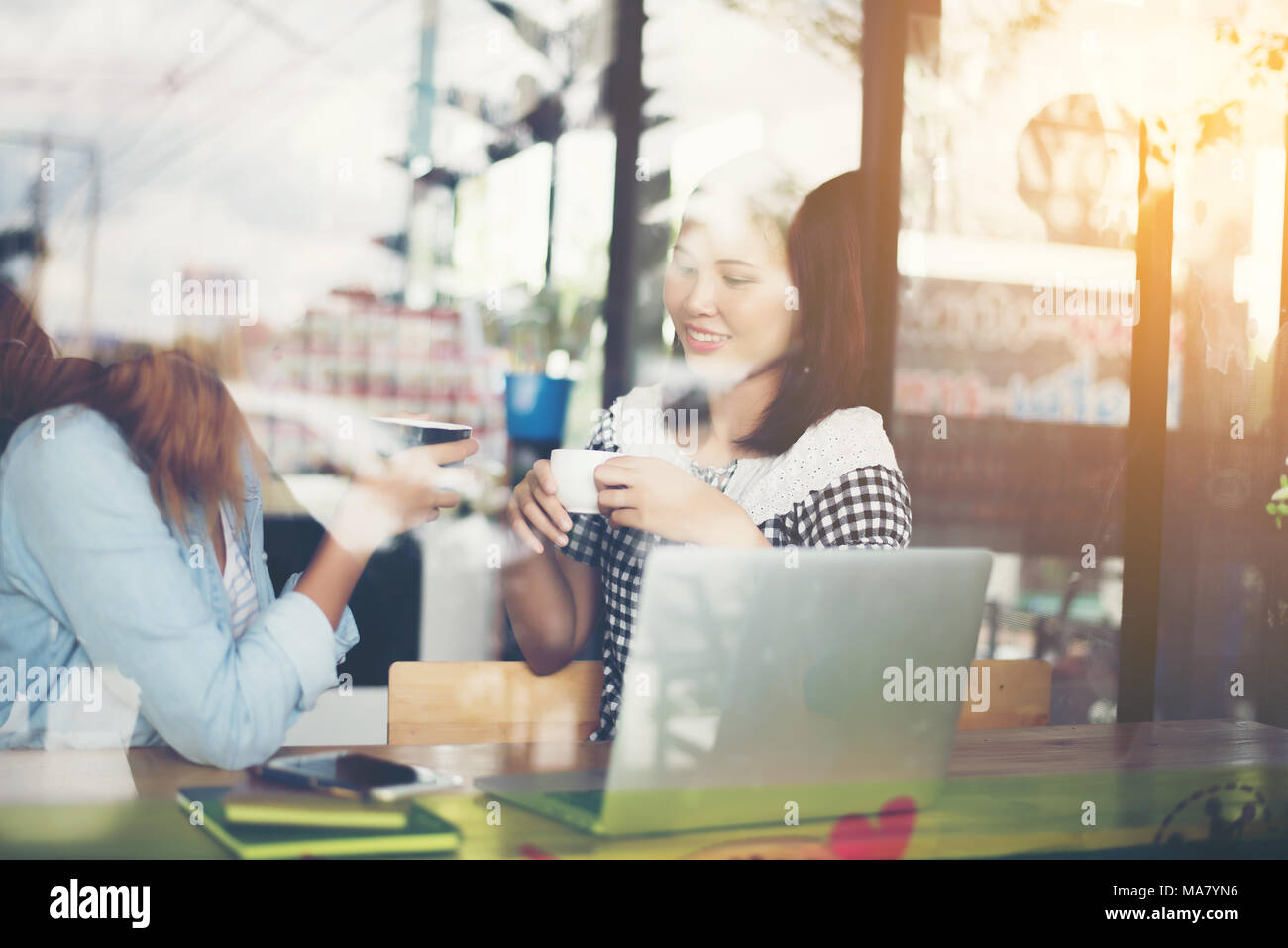 Two friends enjoying working together with window reflection in a ...