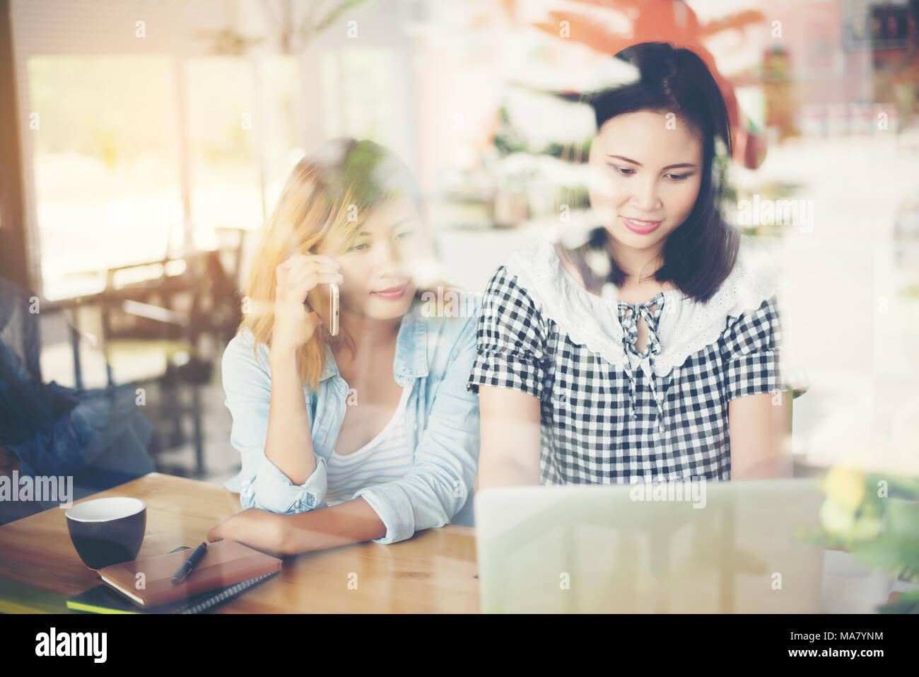 Two friends enjoying working together with window reflection in a ...