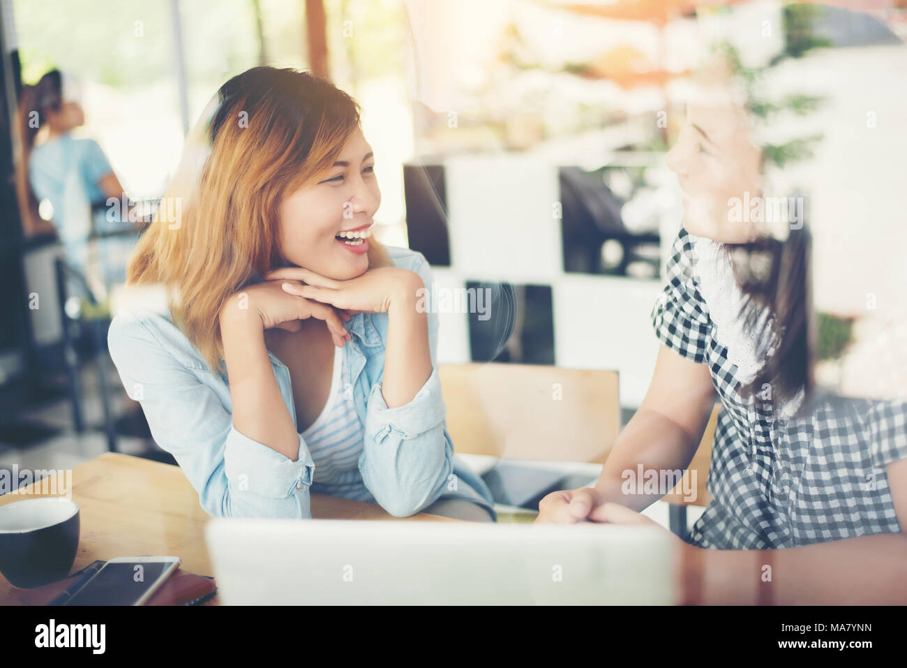 Two friends enjoying working together with window reflection in a ...