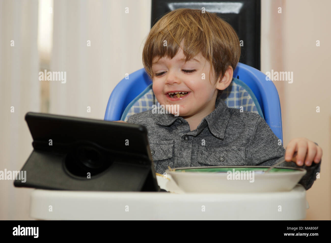Young boy watching an electronic tablet while eating.Credit: Mario ...