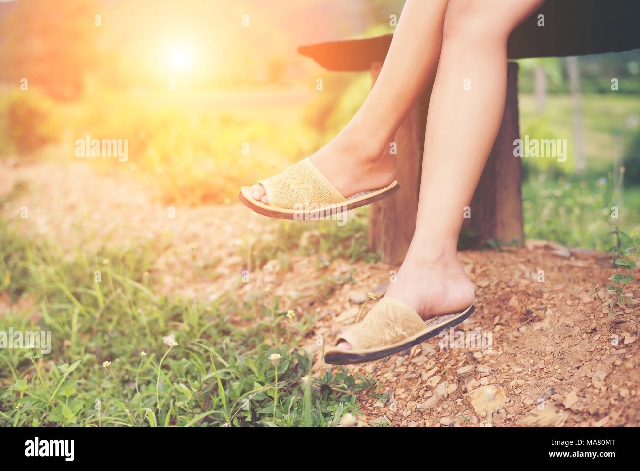 Legs of a beautiful woman sitting on a bench amidst flowers and nature ...
