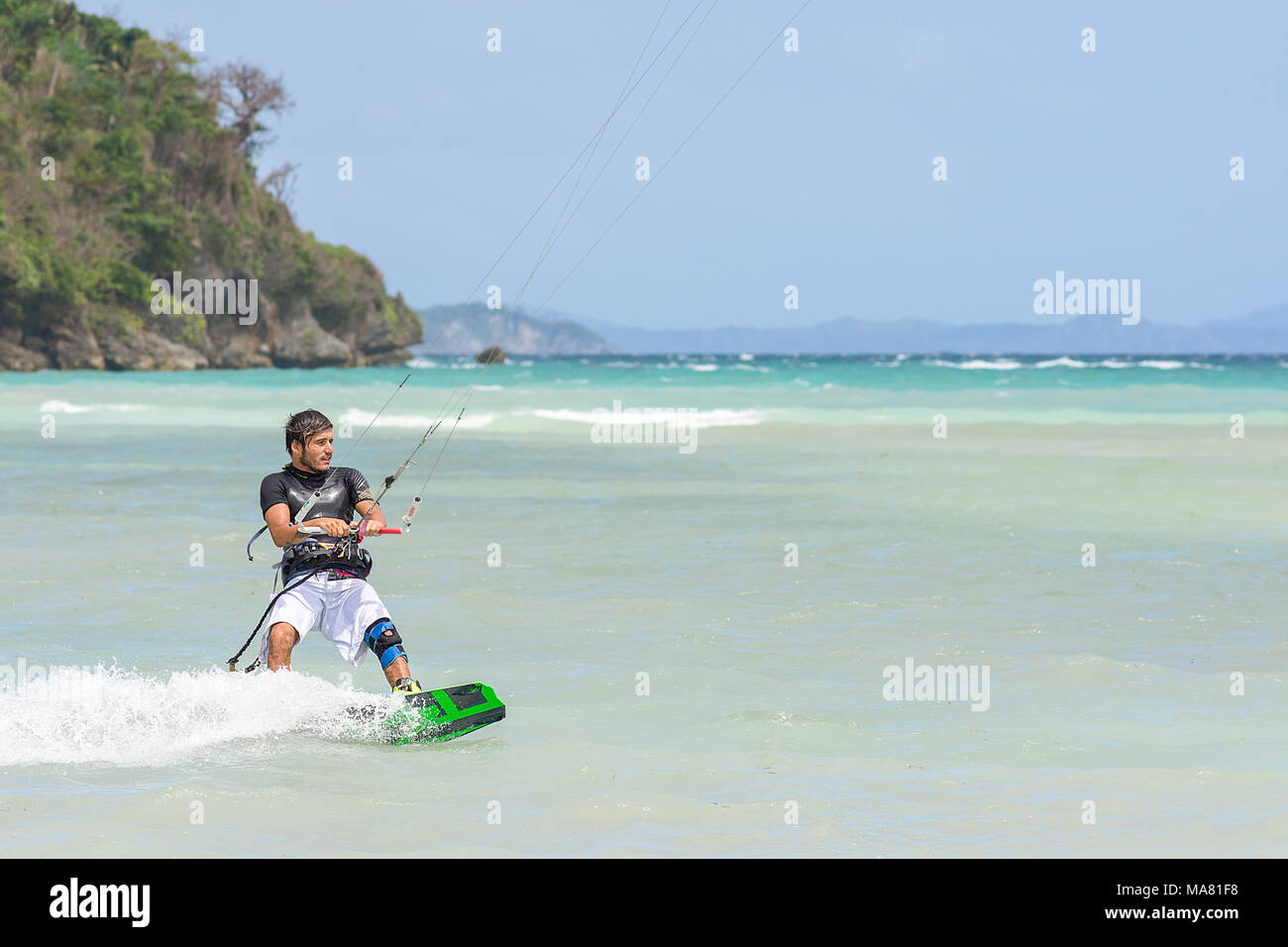 A young male kite surfer rides his board and kite in the shallow clear ...