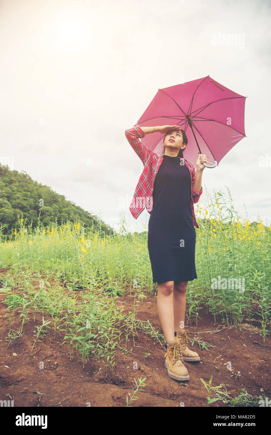 Young beautiful woman holding red umbrella in Yellow flower field and ...