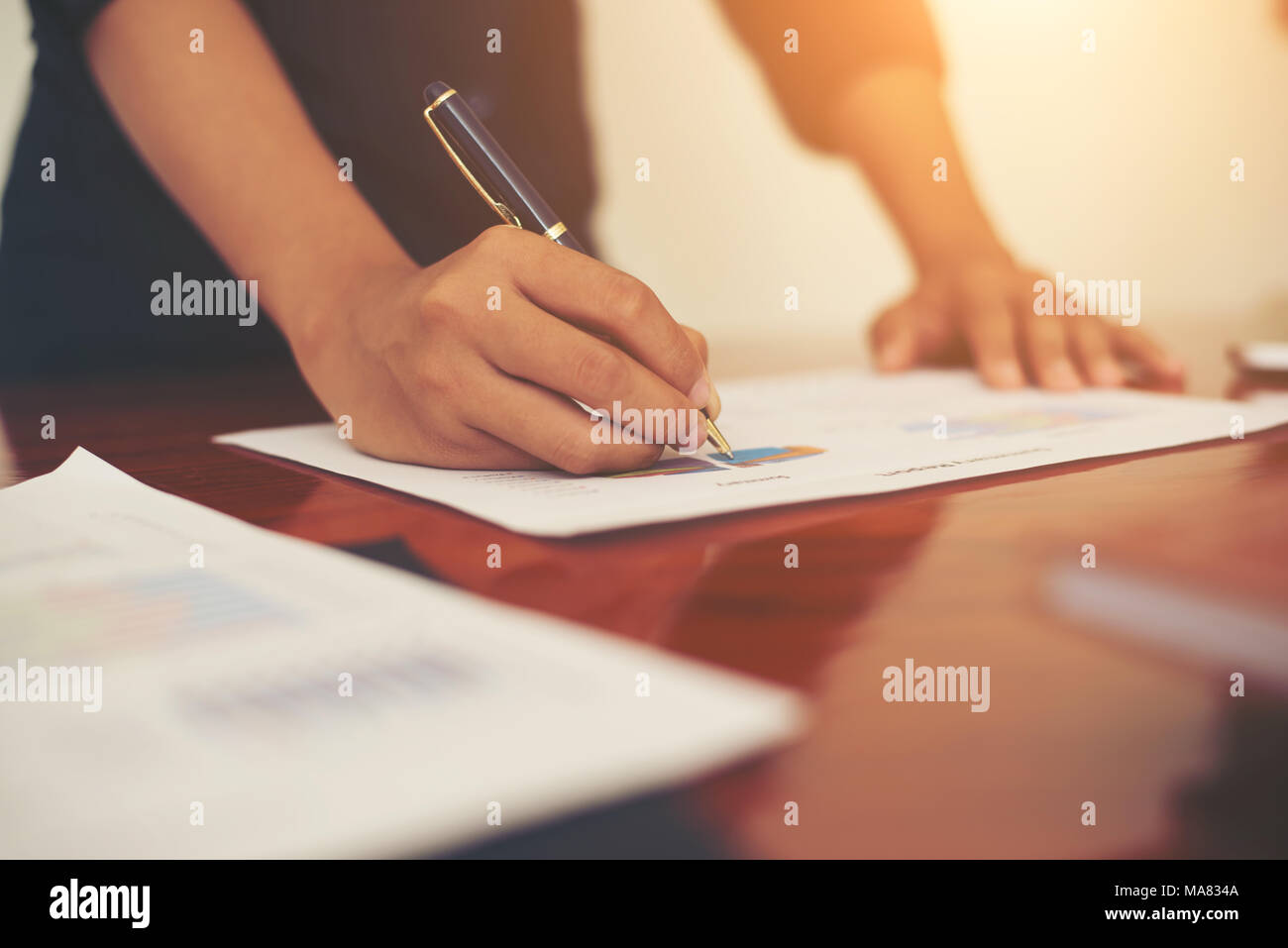 Woman's hand with a pen writing on the business paper. Report chart ...