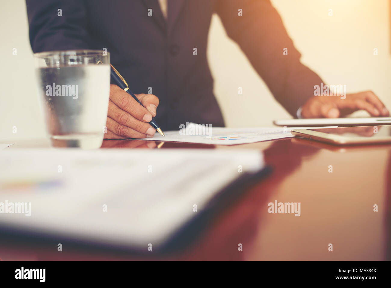 Businessman's hand with a pen writing on the business paper. Report ...