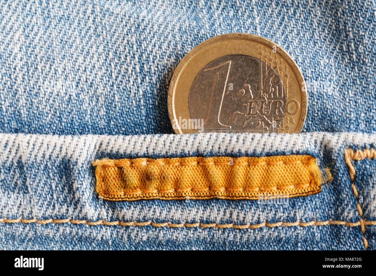 Euro coin with a denomination of 1 euro in the pocket of worn old blue ...
