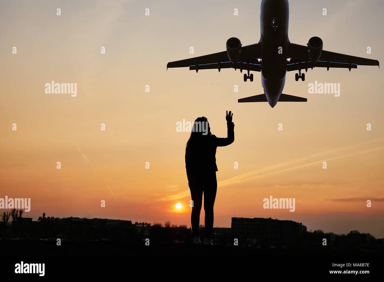 Girl wave to the plane with sunset background Stock Photo - Alamy