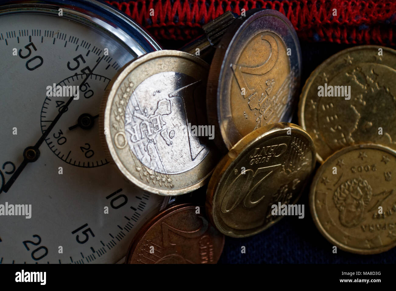 Pile of euro coins with old vintage stopwatch on blue jeans background ...