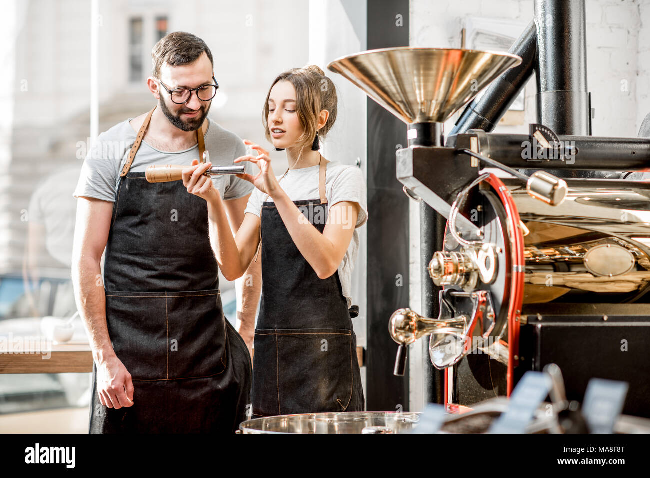 Couple of baristas in uniform checking the quality of roasted coffee beans standing near the ...