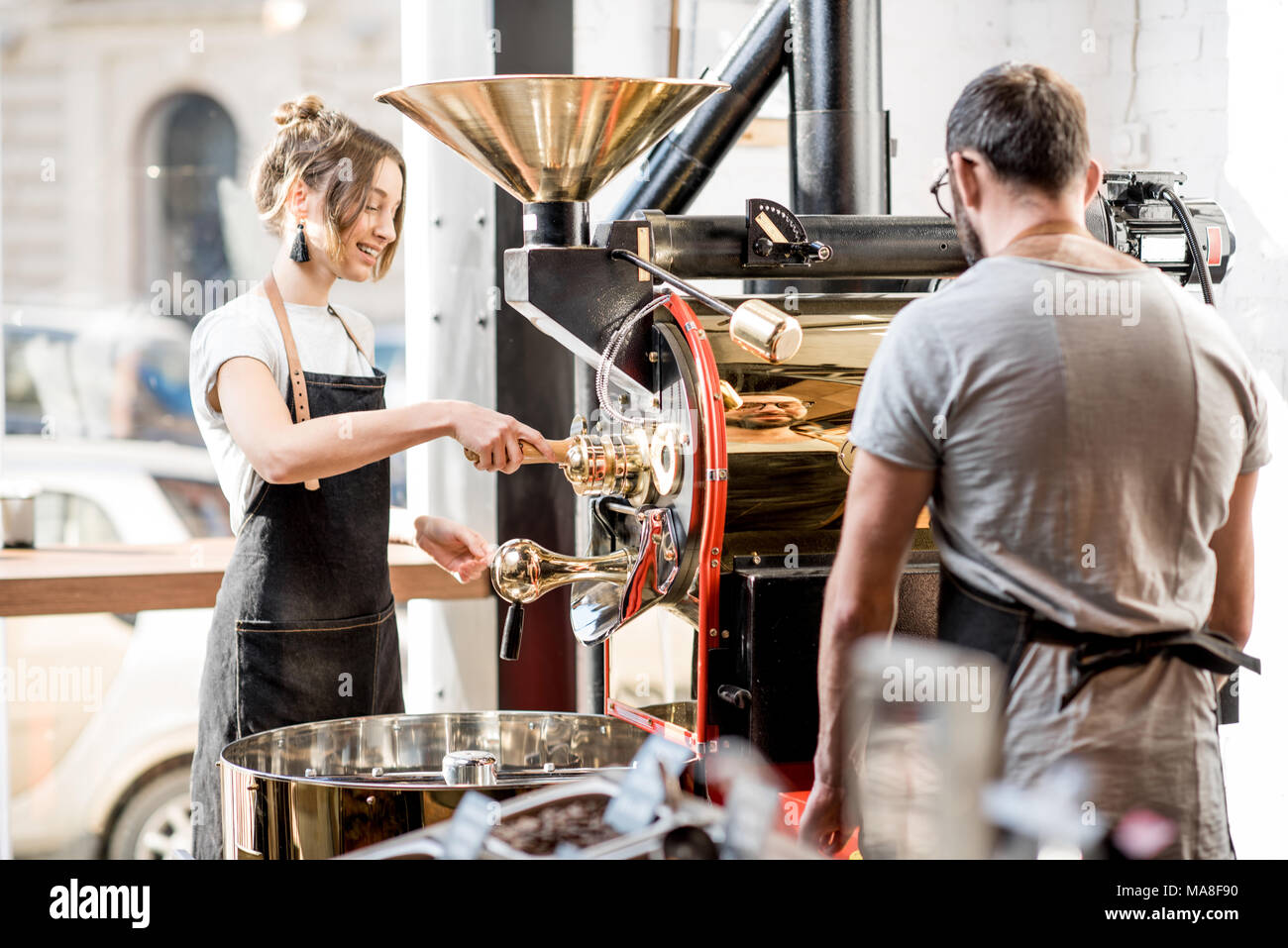 Man and woman in uniform working with roaster machine roasting coffee ...