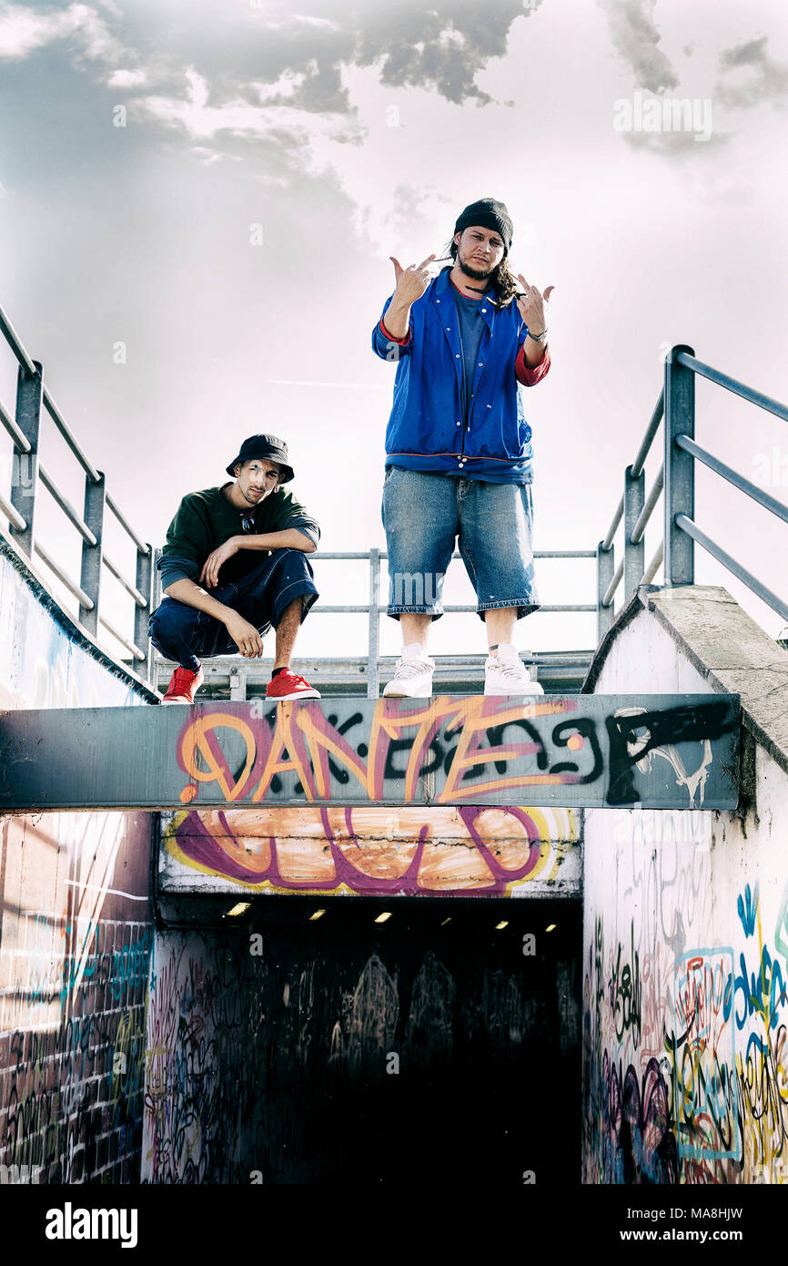 Two rap singers on a concrete beam with graffiti in the background ...
