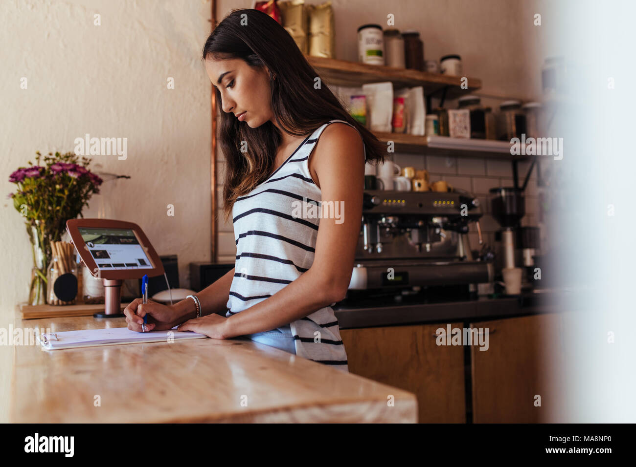 Woman standing at the billing counter of her cafe noting orders ...