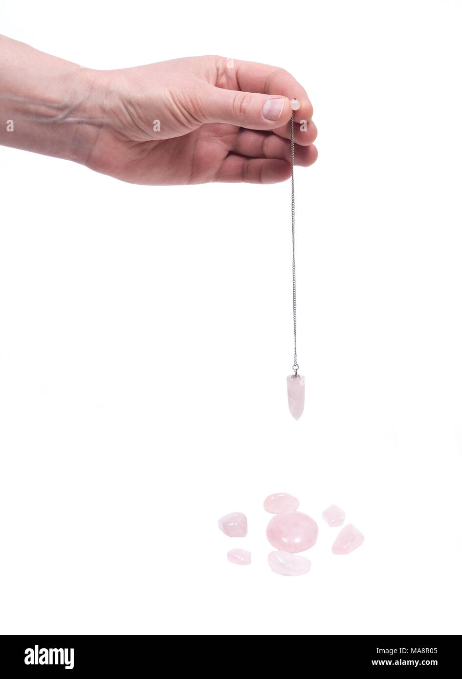 Young woman's hand holding rose quartz pendulum over tumbled rose ...