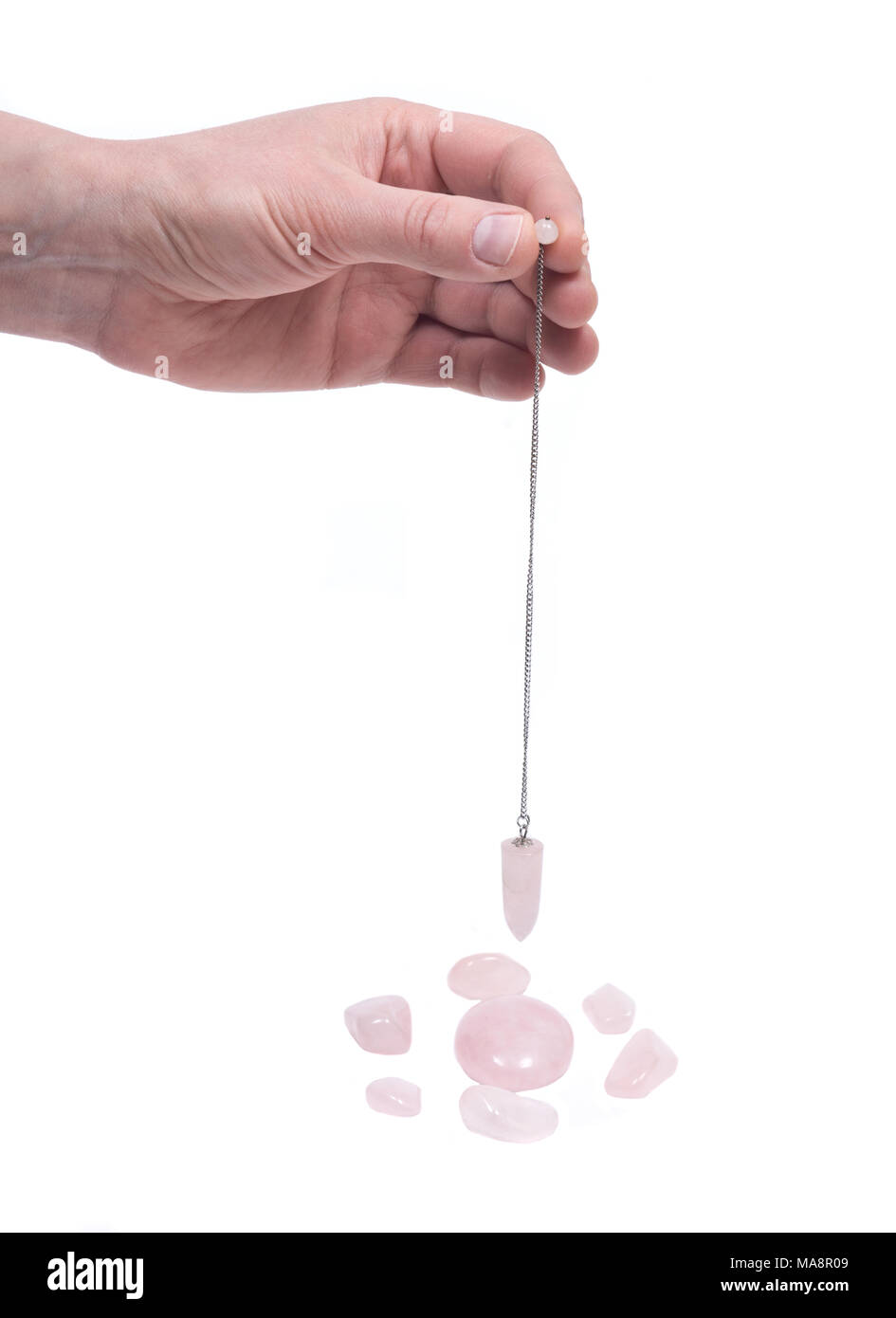 Young woman's hand holding rose quartz pendulum over tumbled rose ...