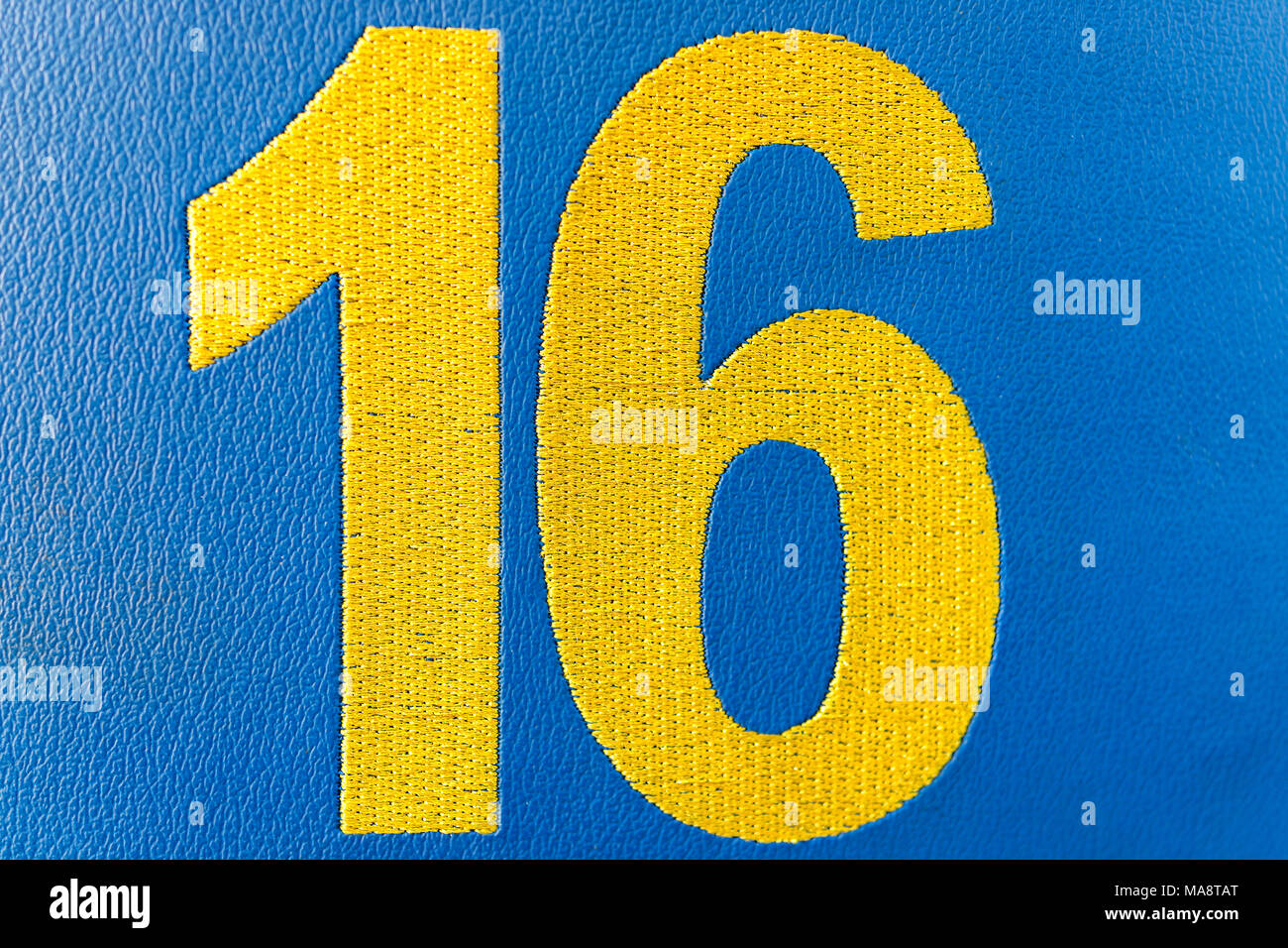 Closeup of woven sixteen 16 number on cloth against bright vibrant blue ...