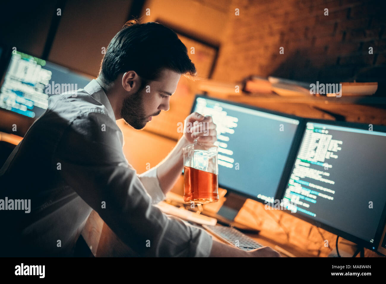 Loser man drinking alcohol at workplace. Indoor, studio shot. Hacker ...