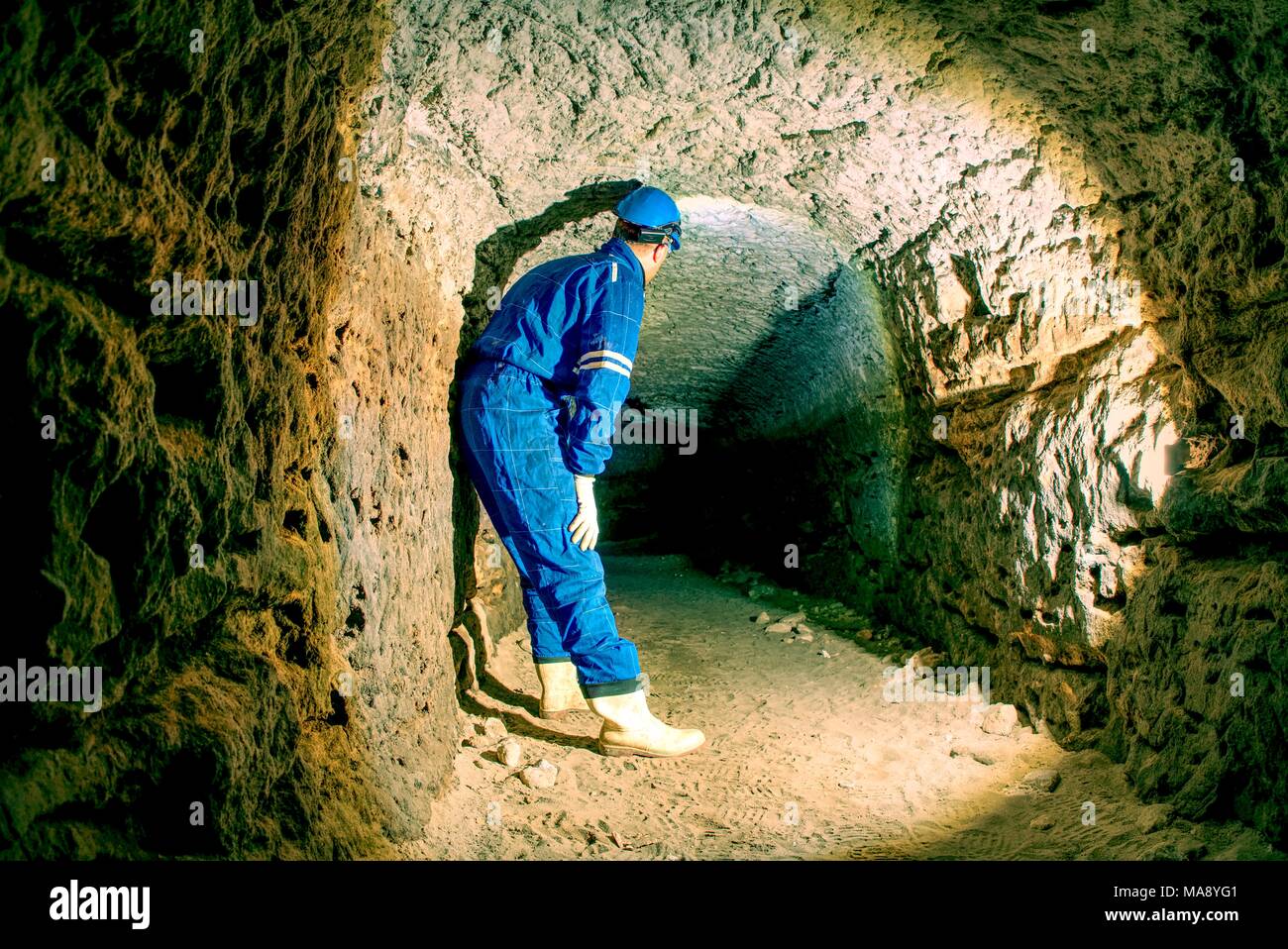 Hunched worker in a blue overall and a safety helmet work in ...