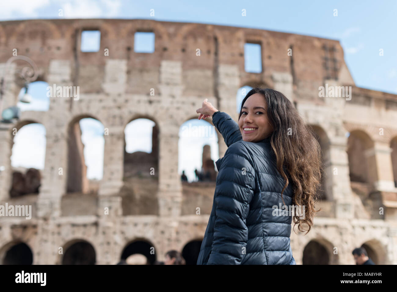 Long black hair and smiling woman pointing to the Colosseum, important ...