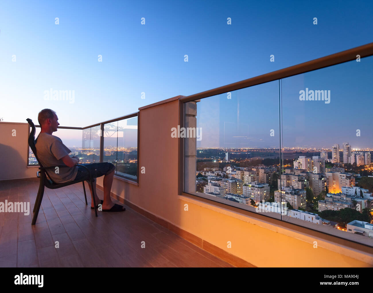 Man on high end balcony in downtown of modern city.Scape of evening ...