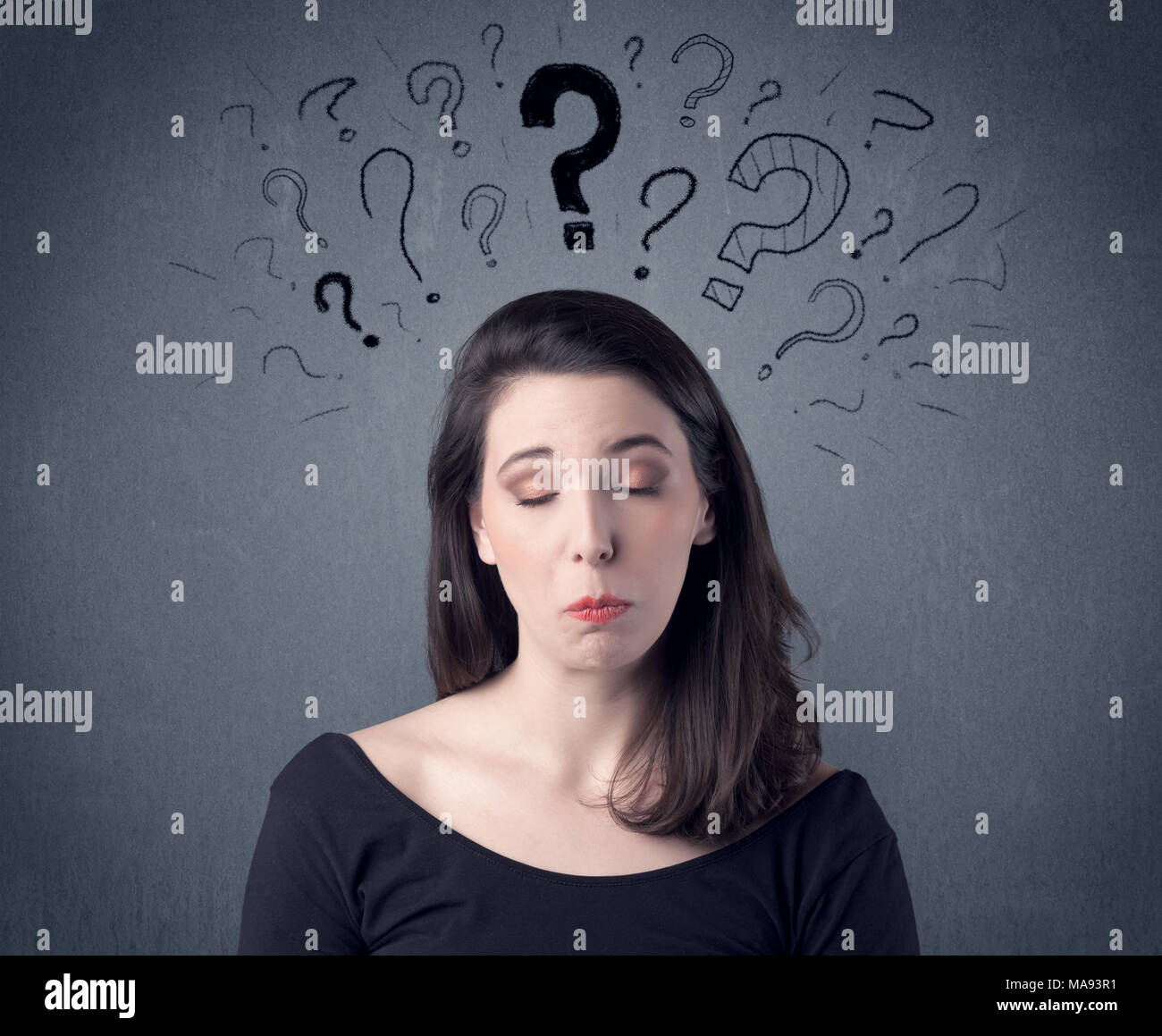 A pretty teenage girl standing confused in front of grey wall ...