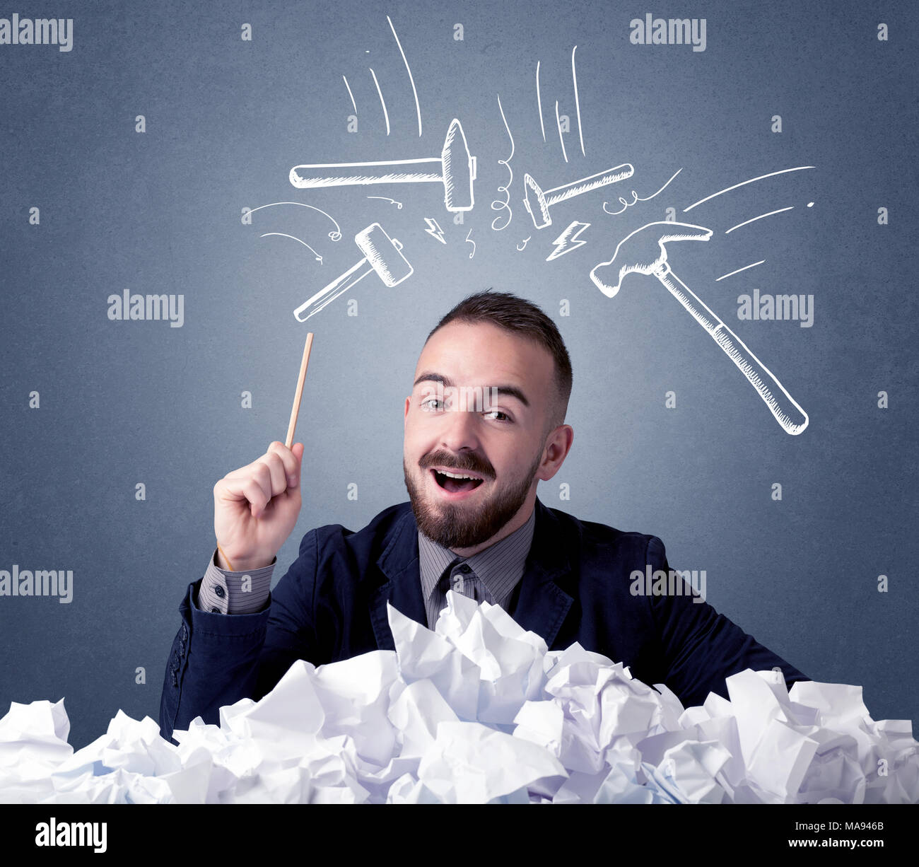 Young businessman sitting behind crumpled paper with drawn hammers ...