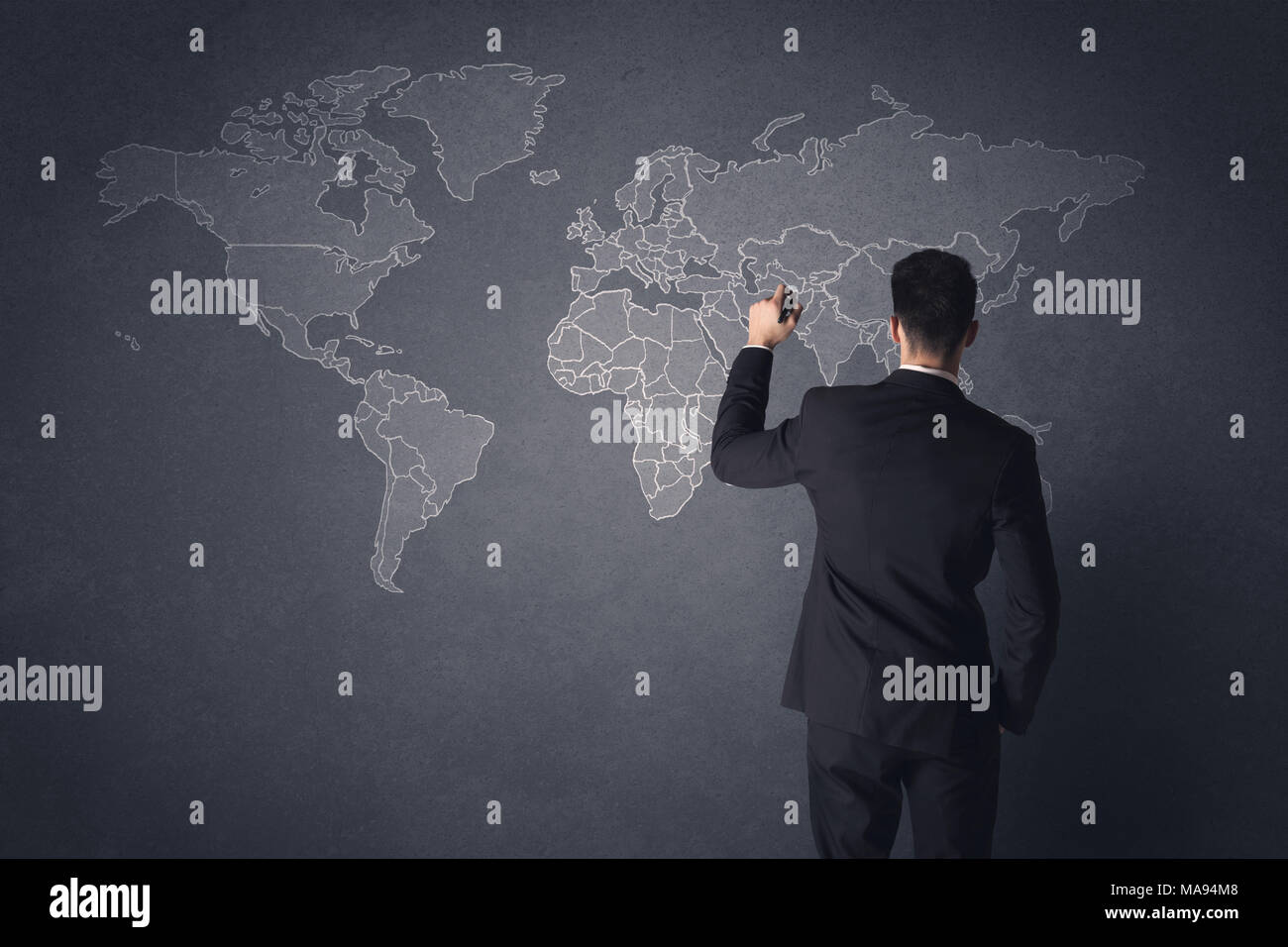 Young businessman in black suit standing in front of a black world map ...