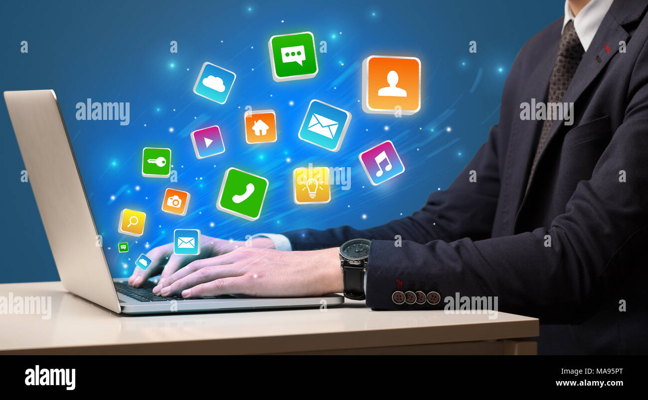 Businessman hand typing on laptop with flying application icons around ...