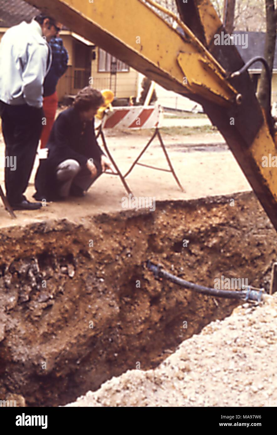 Photograph of two workers standing near an area of ground dug up in ...