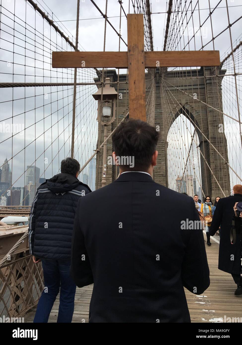 A young adult carries a cross across the Brooklyn Bridge in New York ...