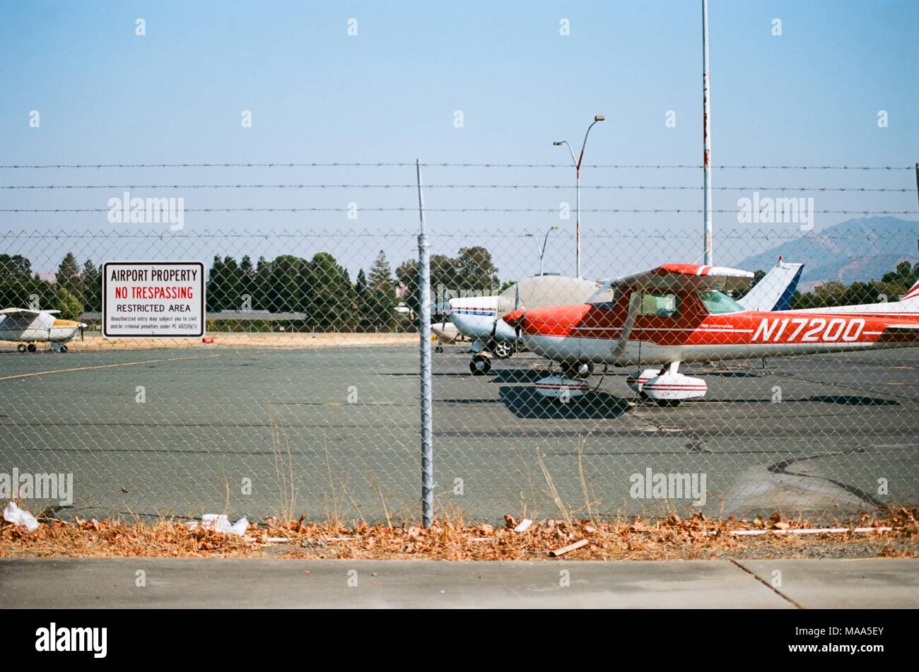 Small private light aircraft are parked on the tarmac behind a fence at ...