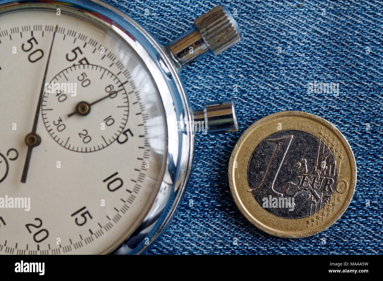 Euro coin with a denomination of one euro and stopwatch on worn blue ...