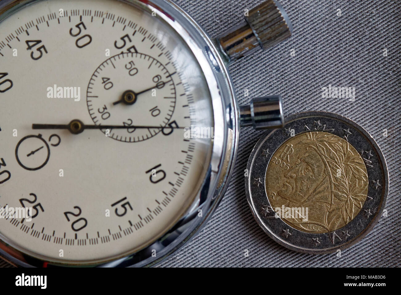 Euro coin with a denomination of 2 euro and stopwatch on gray denim ...