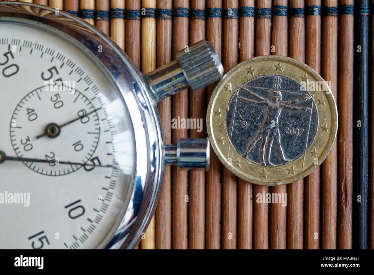 Euro coin with a denomination of 1 euro and stopwatch on wooden table ...